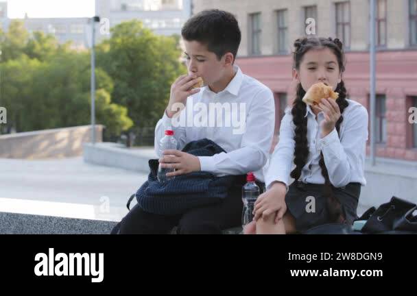 Two children eat buns outdoors during school break, hungry ...