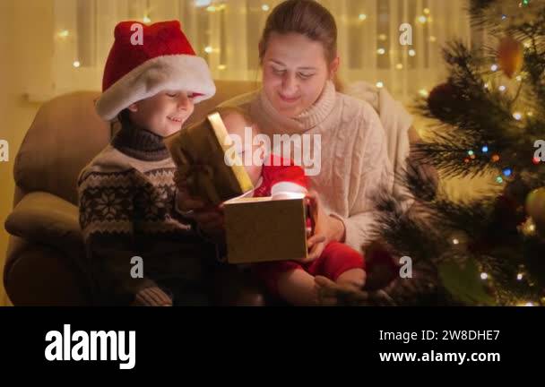 Cute baby boy sitting on mothers lap in armchair and looking inside ...