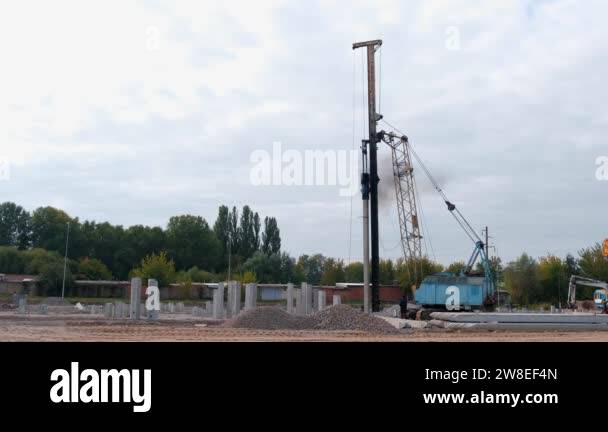 A large vertical piling crane equipped with a diesel hammer hammers ...