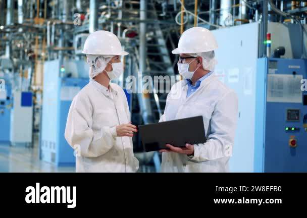 Two factory workers in lab coats are talking. Engineers, teamwork ...