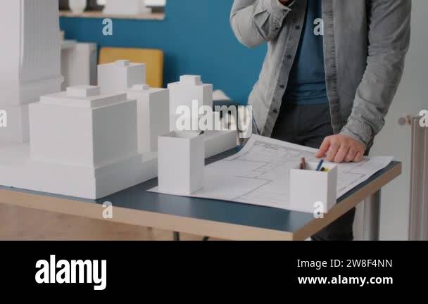 Close Up Of Architect Taking Notes On Blueprints Plan To Work On Building Model And Maquette