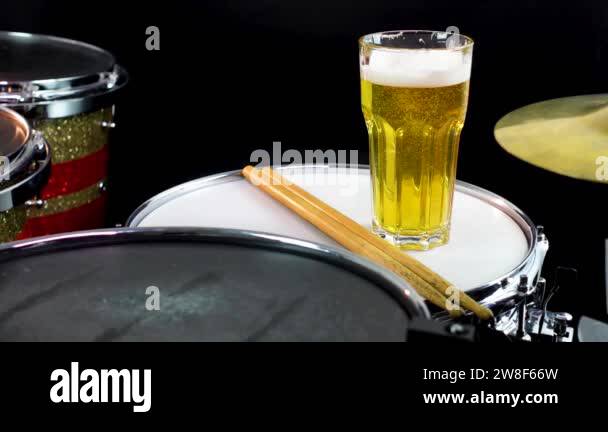 Glass of light beer on professional drum set closeup. Drumsticks, drums ...