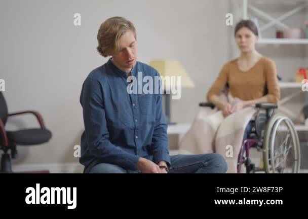 Overwhelmed Caucasian young man with blurred angry disabled woman in ...