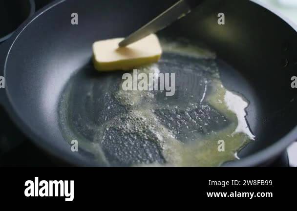 Piece of golden butter slowly melts in heated black frying pan on ...