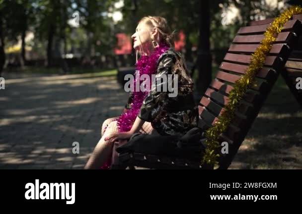 Side view drunken young woman singing sitting on bench in sunshine ...