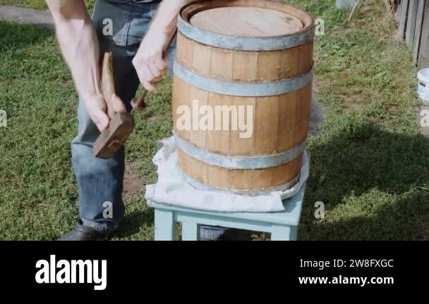 Man opens an oak barrel, knocking with a chisel and a hammer on an iron ...