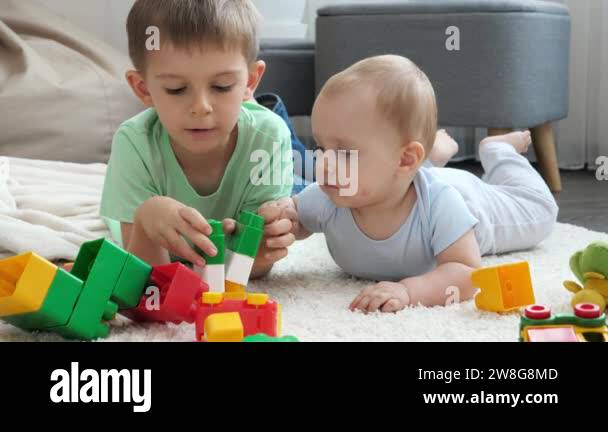 Little boy with baby brother building tower from toy blocks and bricks ...