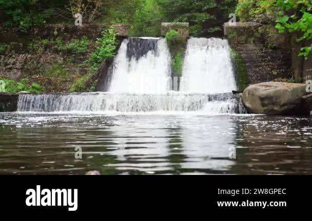 Two waterfalls running over concrete slope and splashing in lake ...