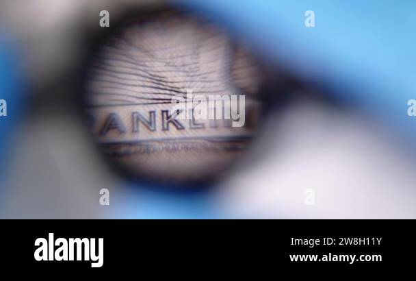 Person examines hundred dollar bill through magnifying glass slow ...