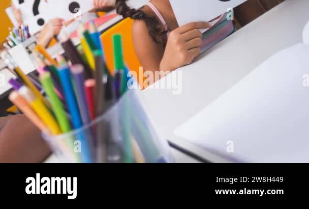 Diverse class of elementary schoolchildren at their desks holding ...