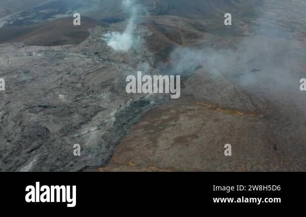Forwards fly above cooled lava stream releasing white smoke. Tilt up ...
