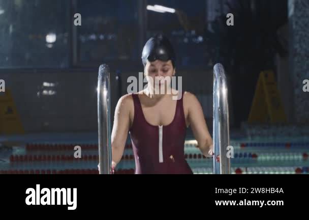 Young woman swimmer in red swimsuit comes up from the water in the pool ...