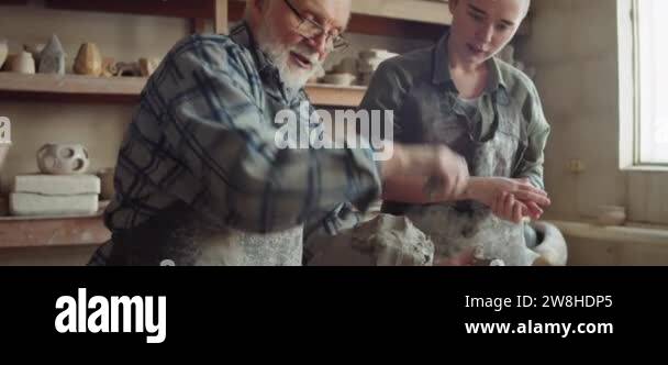 Elderly sculptor forming clay head and giving lesson to young female ...