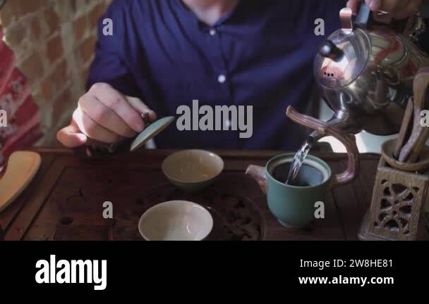 A man pours boiling water from a teapot into a teapot for tea brewing ...