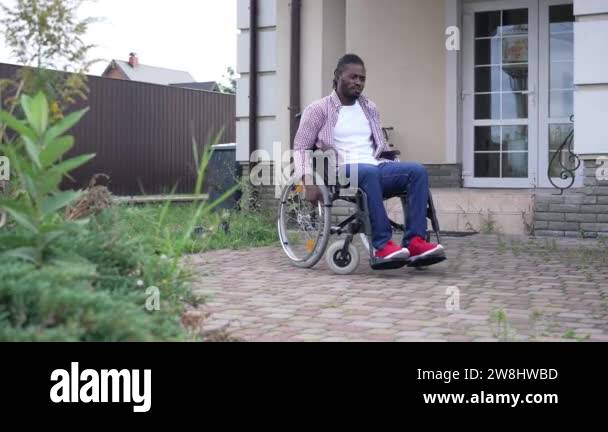 Wide shot troubled stressed African American man rolling wheelchair ...