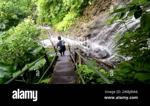 a man descends the iron stairs to a waterfall in the rainforest. An ...