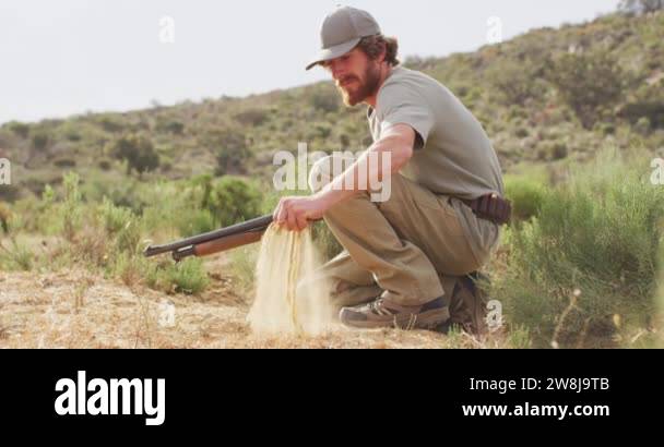Kneeling caucasian male survivalist holding hunting rifle, examining ...
