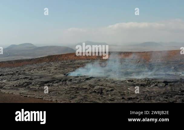 Fly over large hole in cooling lava layer emitting smoke. Volcanic ...