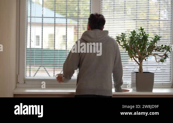 man looking out his window at home in the kitchen and drinks coffee ...