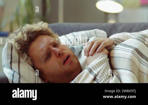 Feverish Man With Sweaty Forehead Lying Under Blanket At Home Coughing