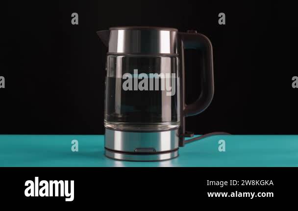 A modern glass electric kettle, on a blue table, black background ...