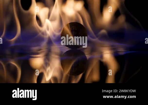On a black background, a flame ignites and illuminates a gold bitcoin ...
