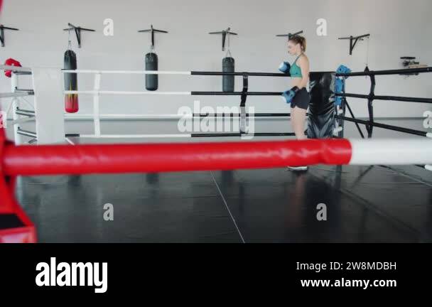 Flexible young woman boxer stretching legs after training inside boxing ...