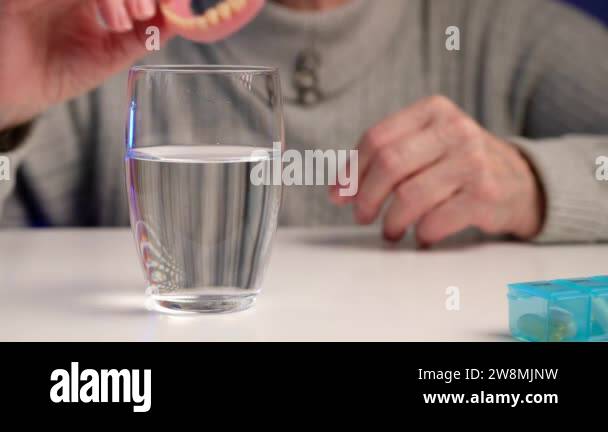 Elderly woman takes false teeth out of her mouth and puts it in glass ...