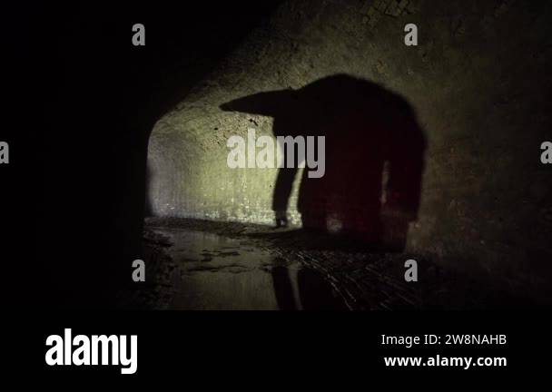 A man with a red lantern walks in an old brickwork underground drain ...