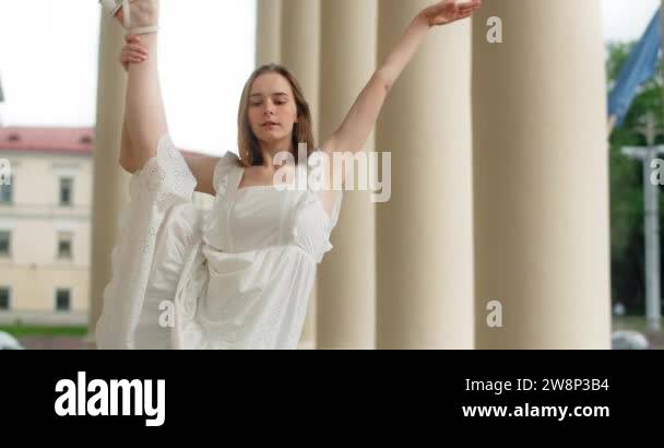 Young dancer woman in white dress whirls in the gallery of columns ...