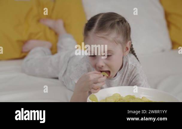 little child eating potato chips lying on bed in bedroom, delicious ...