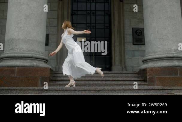 Young dancer in white dress dances on the stairs of the theatre in slow ...