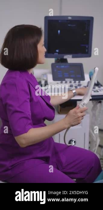 Vertical video. A female gynecologist in a purple medical suit sits ...