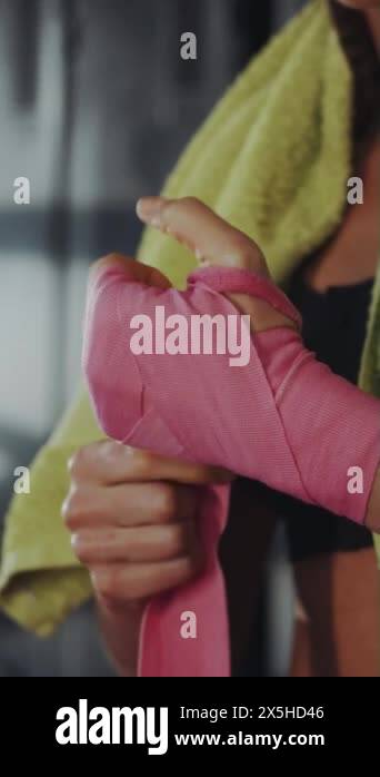 Vertical screen: Woman wrapping her hands with pink boxing wraps, with ...