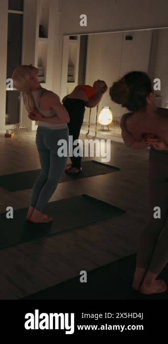 Vertical screen: Women in yoga class perform stretching exercises in ...