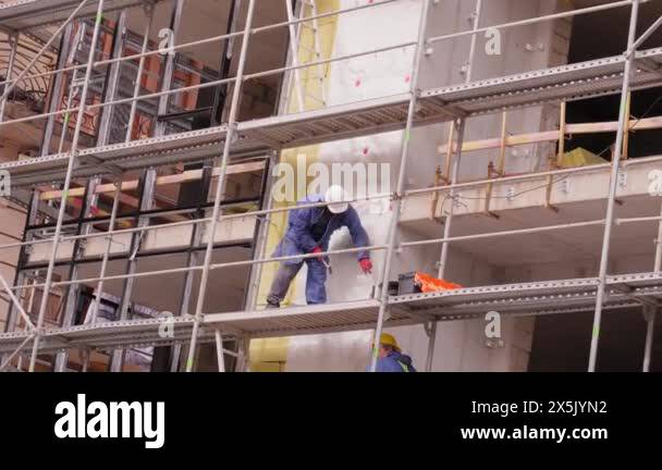 Workers sheathing walls of building facade cladding, walls in house ...