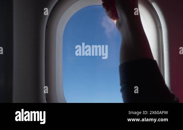 Silhouette of woman hand over the window of airplane. Clouds and sky as ...