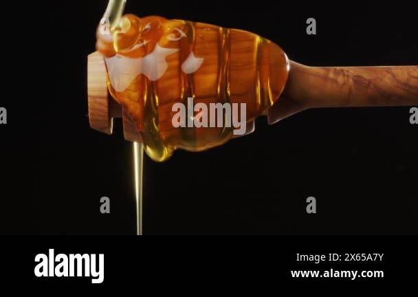 Drops of honey flow from a wooden honey dipper and slowly drip down ...