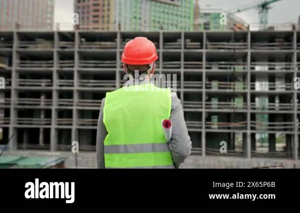 Back view of foreman with blueprints under arm walking up to unfinished ...