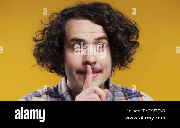 Handsome european brunette guy with curly hairdo shows gesture of shhh ...