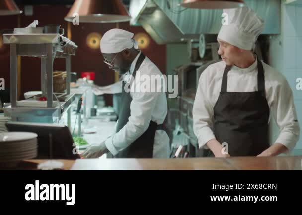 Cheerful Caucasian chef cooking meal, talking with African American ...