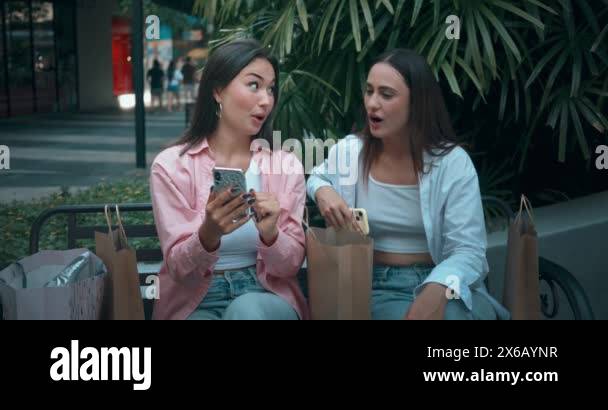 Women friends sitting bench using phones embodying positive ...
