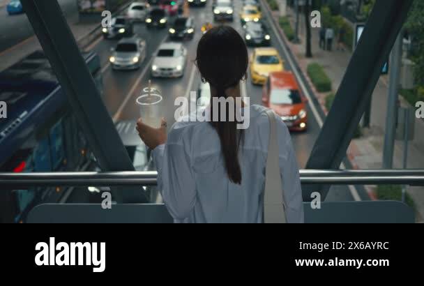 Woman in modern glass overhead crossing looking at traffic urban life ...