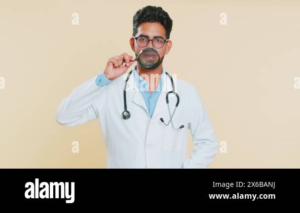 Happy Indian young doctor cardiologist man holding magnifier glass on ...