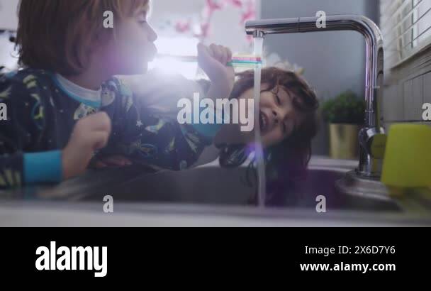 Cute boy with curly hair leans over a kitchen sink to drink water ...