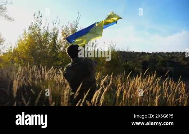 Male military in uniform waving flag of Ukraine at countryside. Young ...