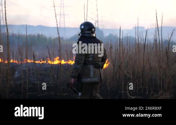 Male firefighter in uniform going with fire hydrant on burnt grass at ...