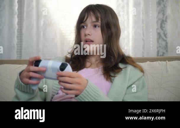 11 years old child holding gaming console and playing on a sofa ...