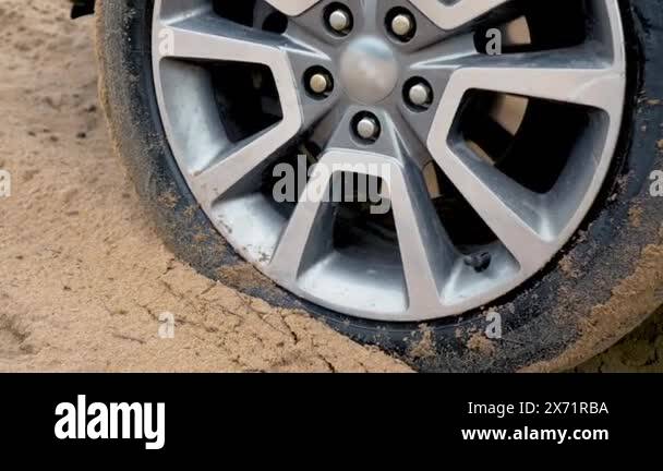Spinning wheel of car stuck in wet sand on dirty country road. Rotating tyres close up. SUV ...