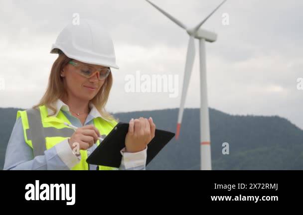 Against the backdrop of the green energy of wind turbines, a woman with ...